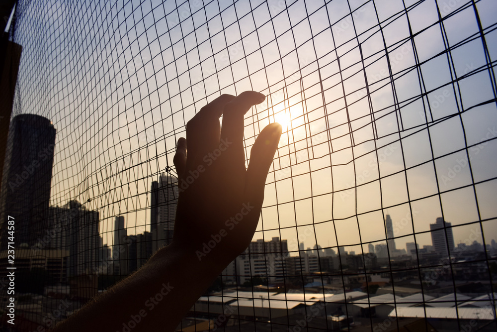silhouette hand holding on iron net cage with blue sky and city ...