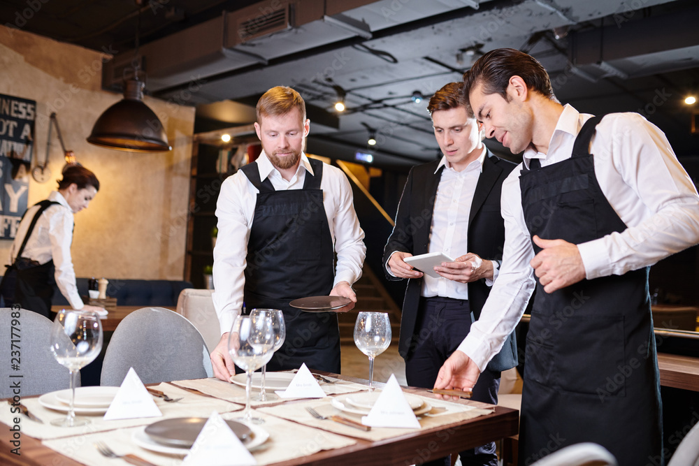 Serious banquet manager and waiters serving tables for event. Handsome ...