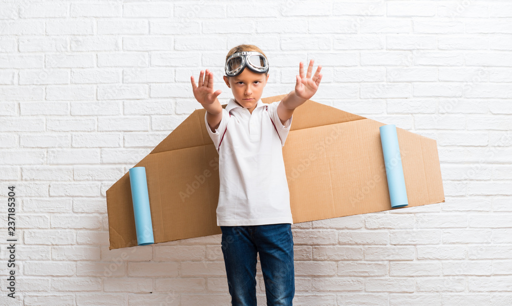 Boy playing with cardboard airplane wings on his back making stop ...
