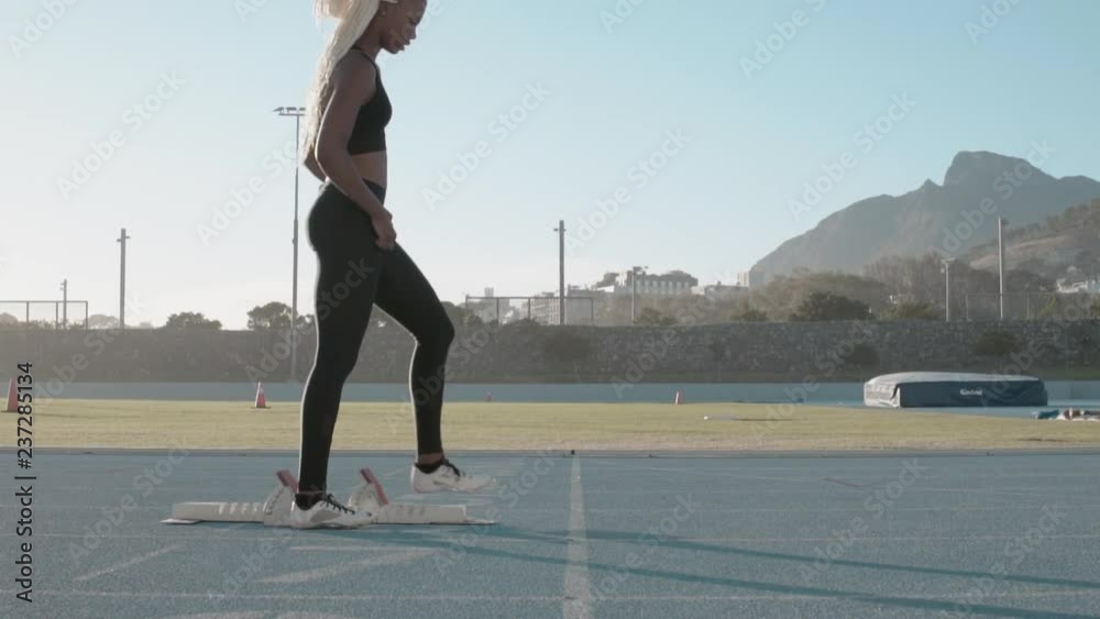 Female athlete taking position on her marks to start off the run ...