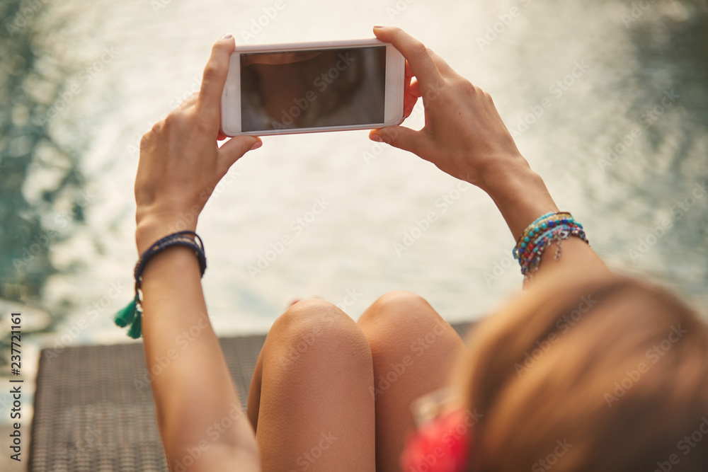 Girl using cellphone while lying on a swimming pool deck lounge bed ...