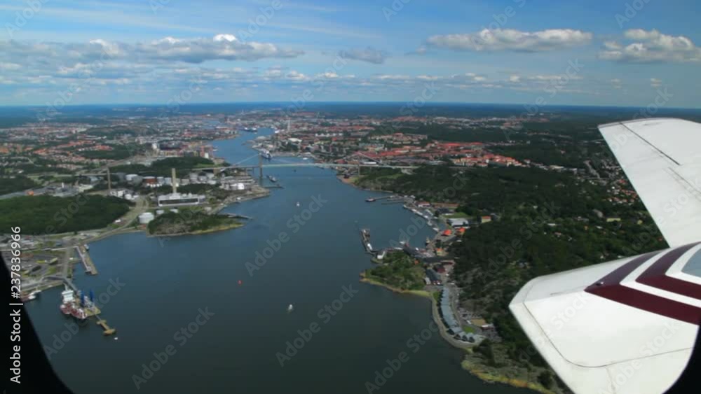 A small airplane flying over land showing a forest, buildings, houses ...