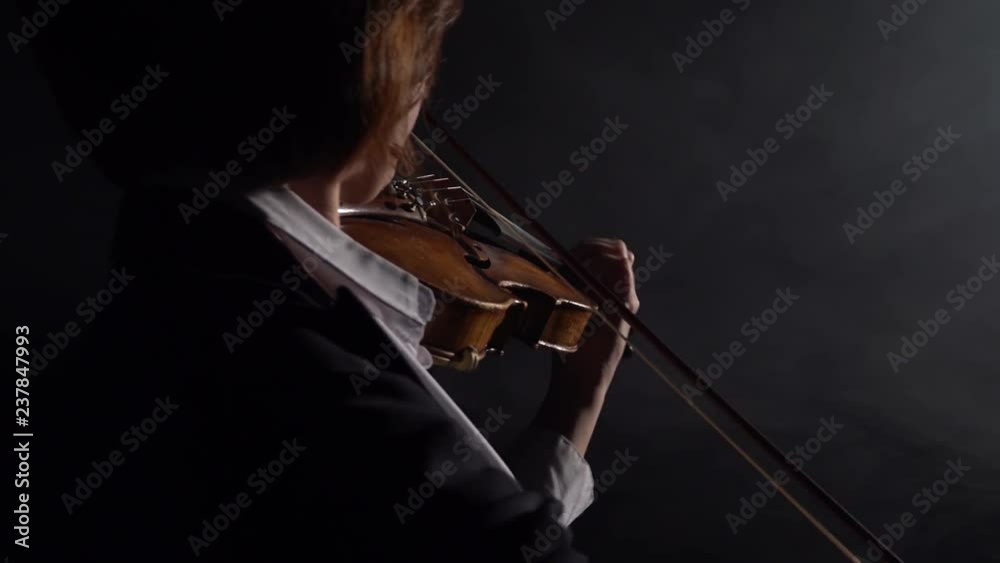 Dark studio where a musician plays the violin while standing with his ...