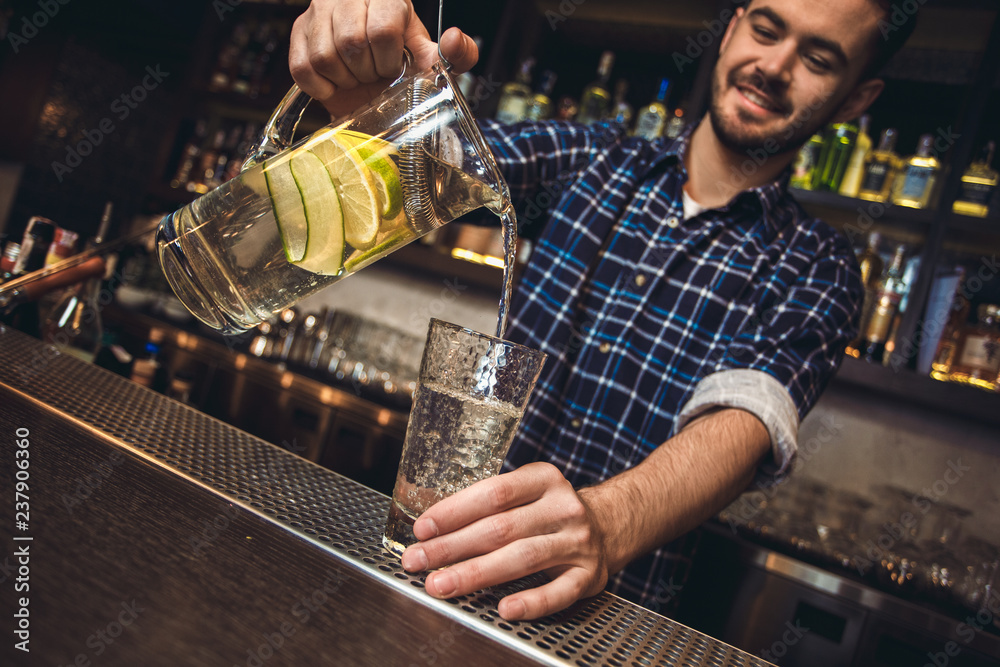 Young bartender standing at bar counter pouring lrmon cocktail into ...