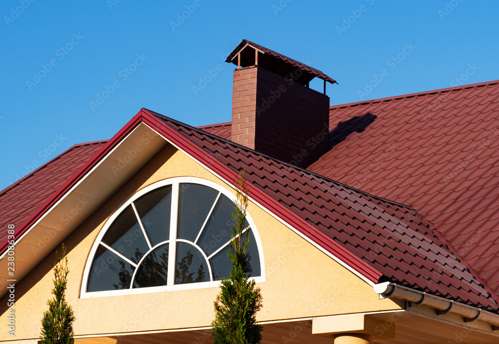 Arched window and brick chimney on the red metal tile roof under blue ...