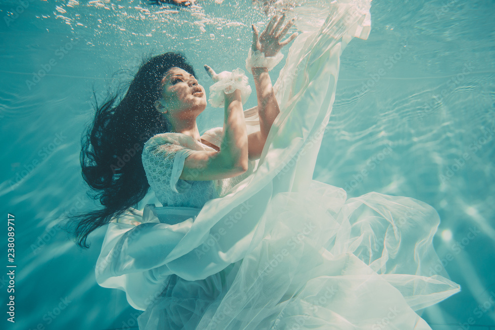 sexy young bride swimming underwater in white wedding dress, stockings ...