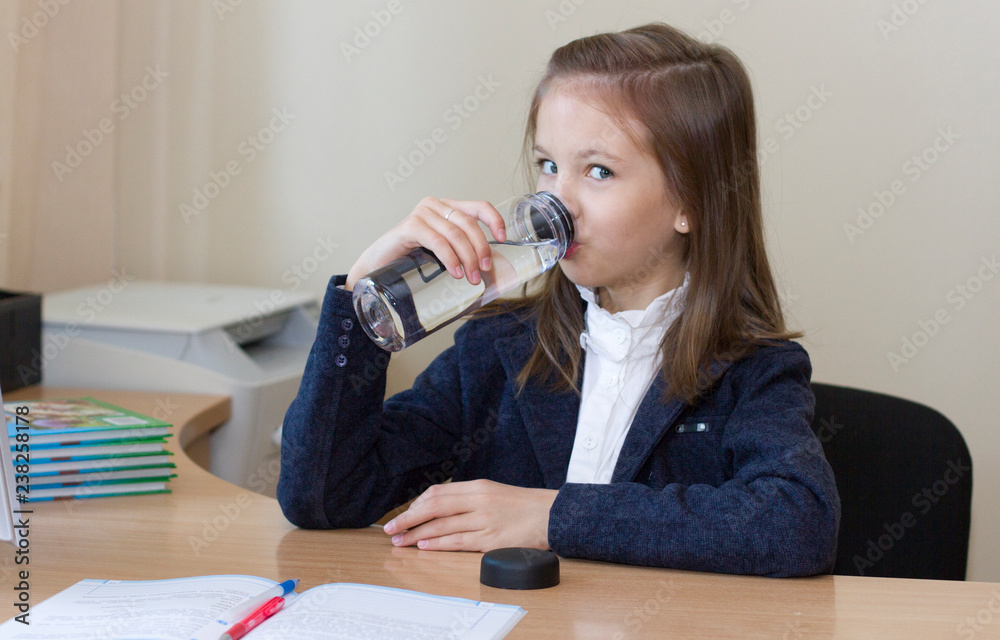 Back to school. A cute girl sits at a desk and drinks water from a ...