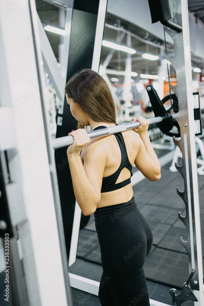 beautiful fitness young girls doing squats with the barbell in smith ...