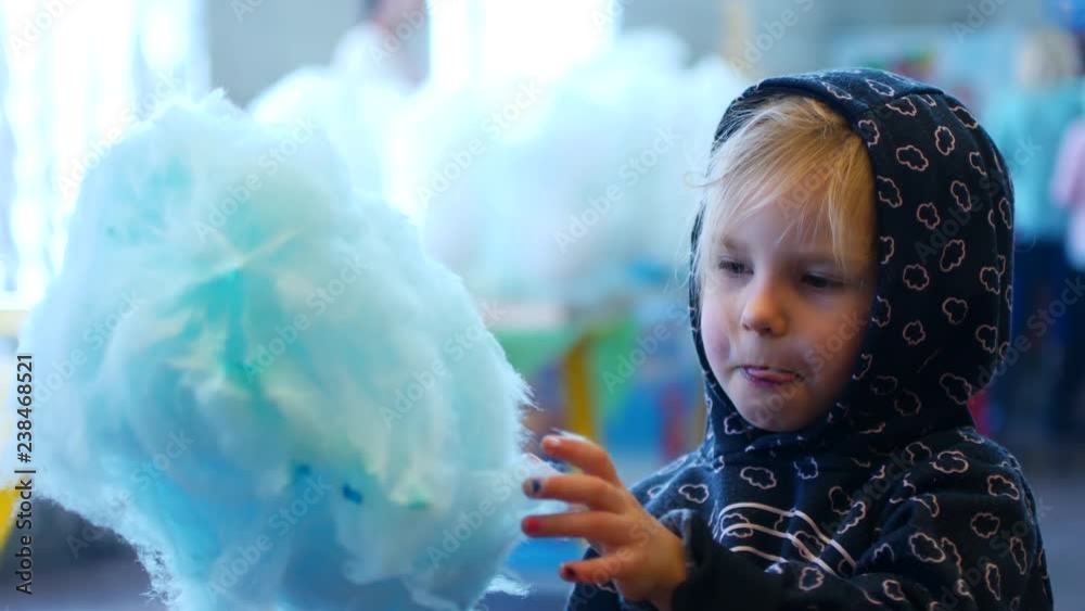 Little girl in the hood eats blue cotton candy in the circus Stock ビデオ | Adobe Stock