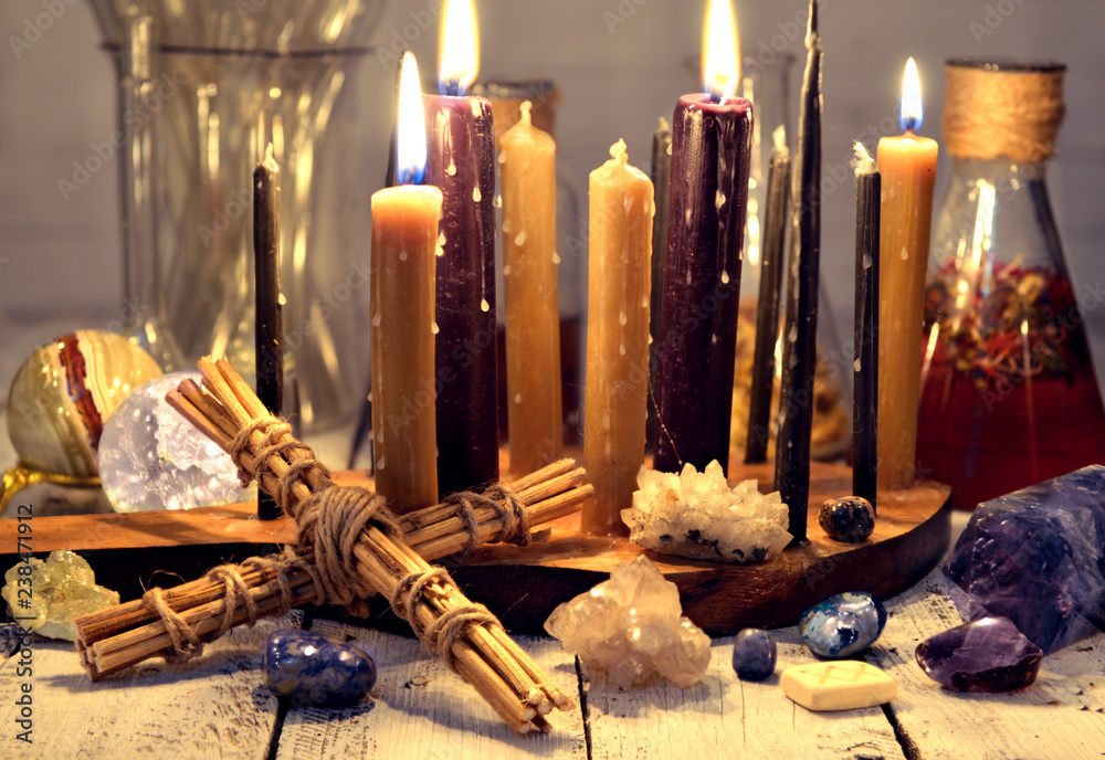 Burning candles, old bottles and flasks, crystals and cross on table ...