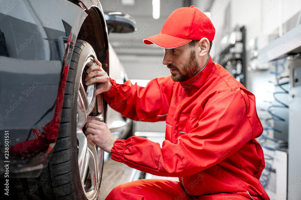 Car service worker in red uniform changing wheel of a sport car at the ...
