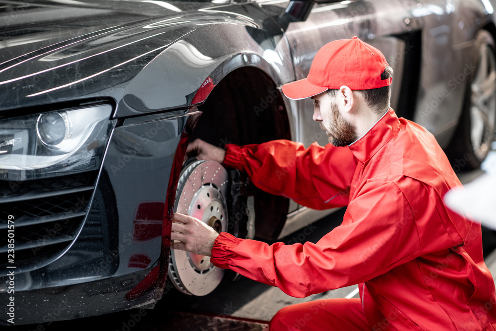 Auto mechanic in red uniform servicing sports car checking front brakes ...