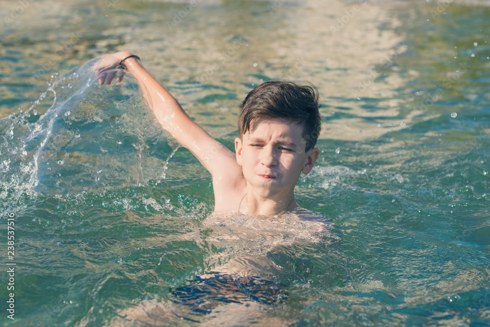 Happy and smiling teen boy swimming on the resort town background ...