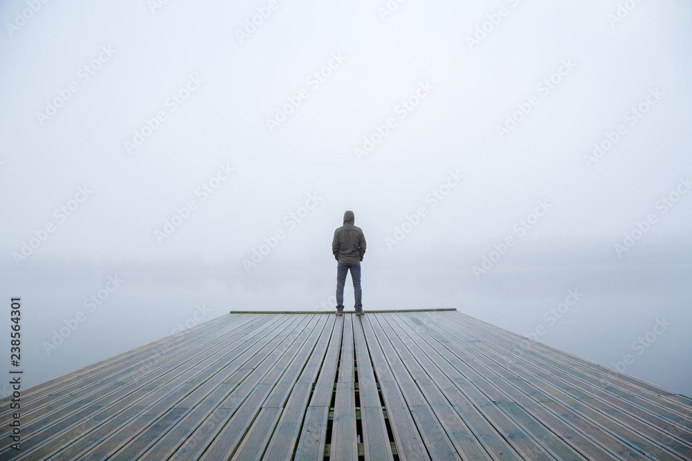 Young man standing alone on edge of footbridge and staring at lake ...