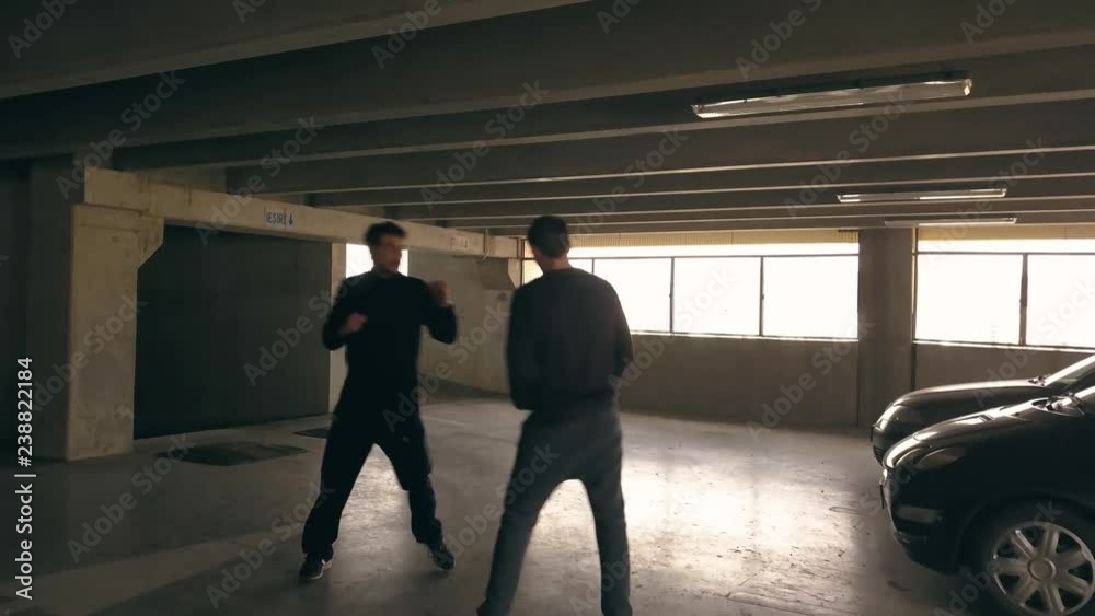 Two men dressed in black rehearse a fight scene in a parking garage ...