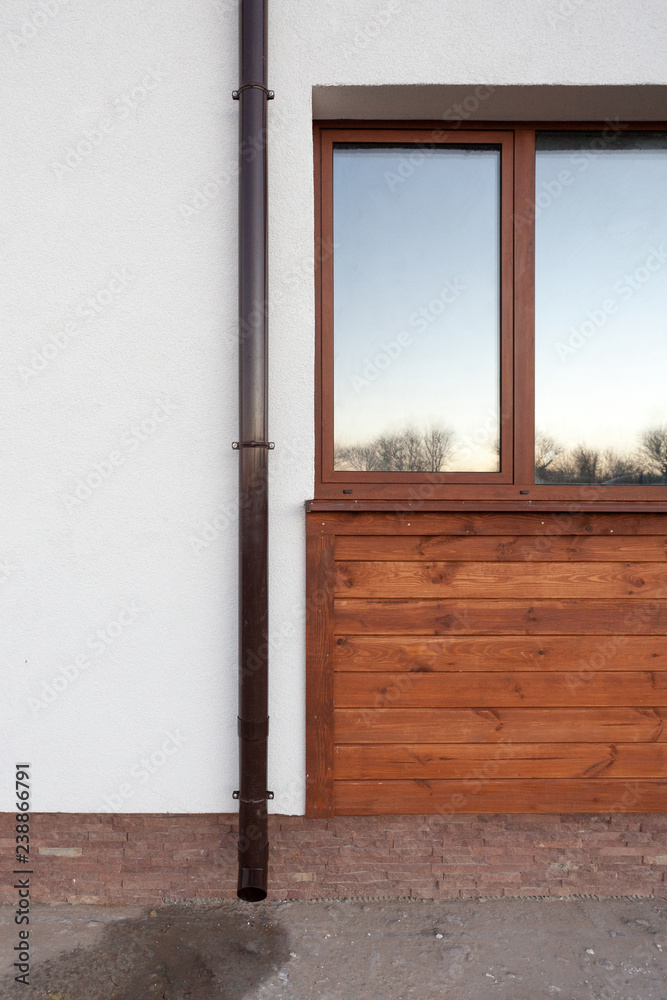 Vertical photo of long brown rain gutter pipe on white wall on new cozy ...