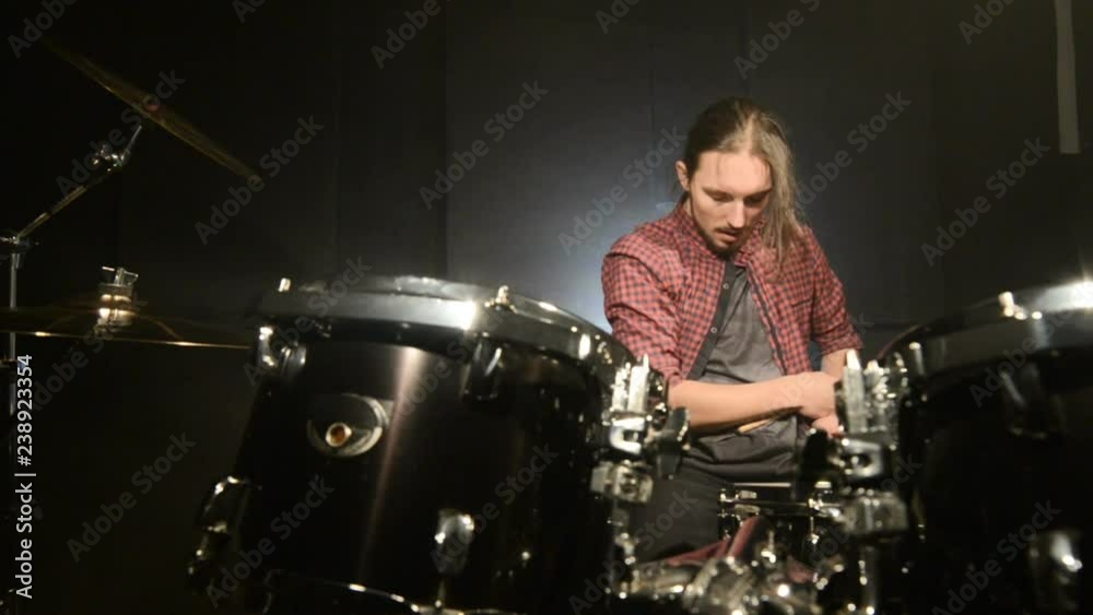 The long-haired drummer finishes playing the drum set in a dark room on ...