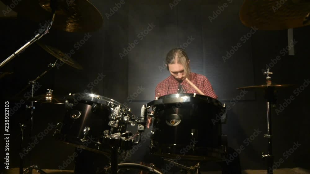 A long-haired drummer sitting at the drum set with drum sticks in his ...