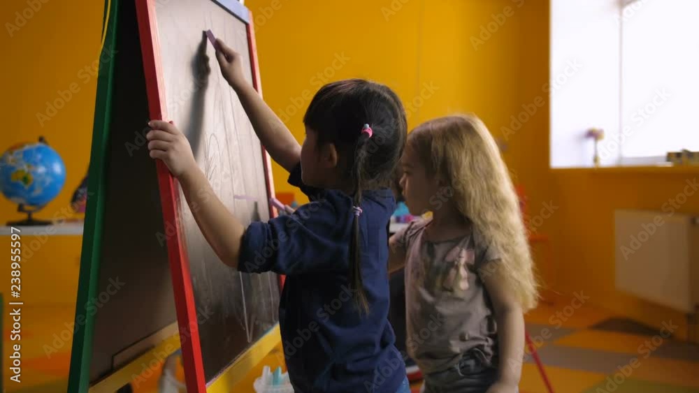 Positive multicultural preschool girls drawing with chalks at ...
