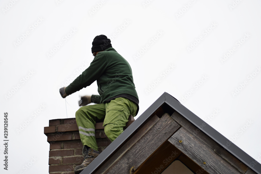Chimney sweep man cleaning brown brick chimney on building roof on ...