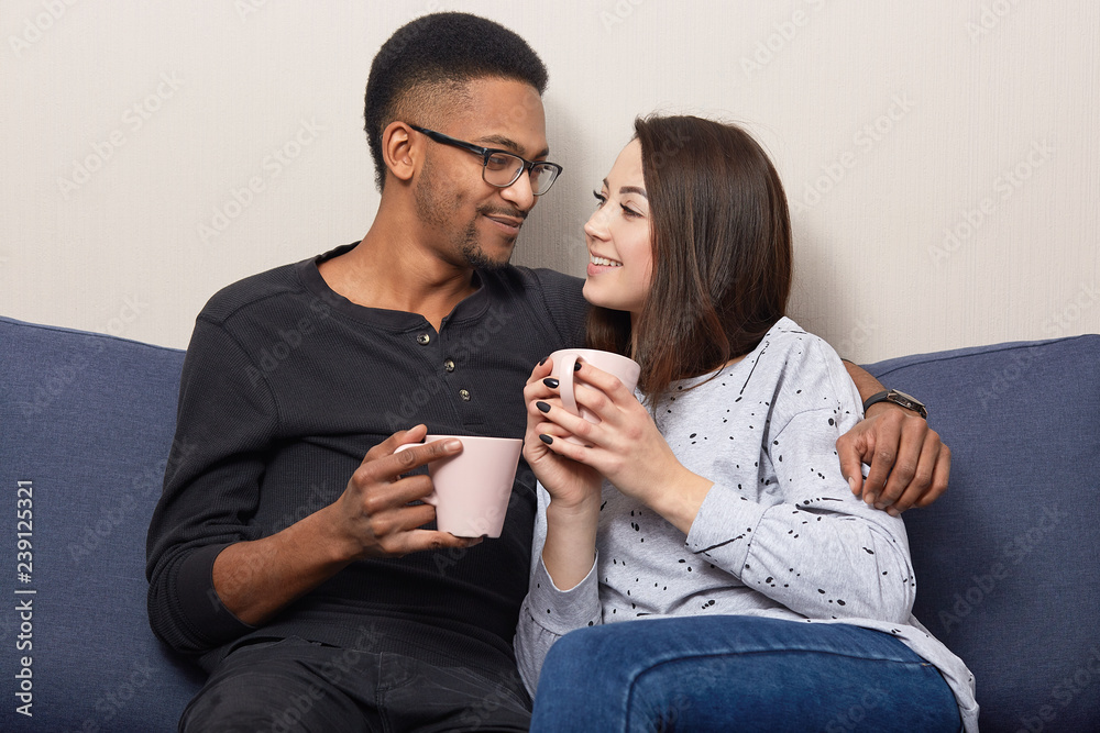 True love concept. Beautiful couple cuddle and pose at sofa, dressed in ...