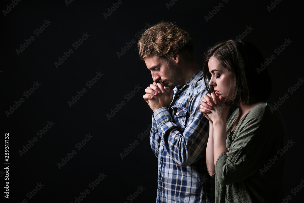 Young praying couple on dark background Stock Photo | Adobe Stock