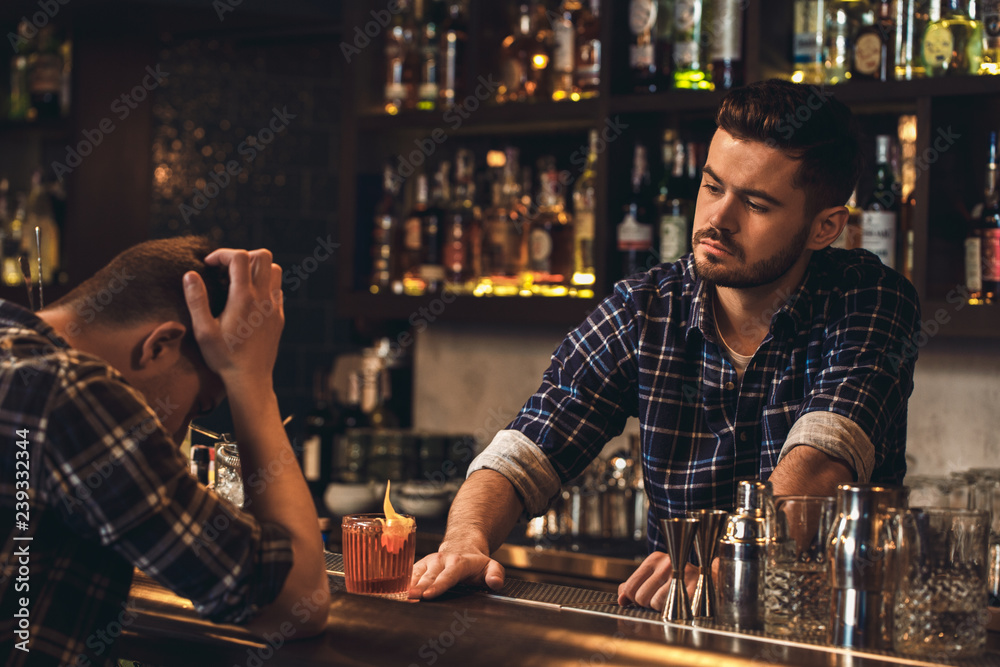 Young bartender standing at bar counter giving cocktail to sad client ...