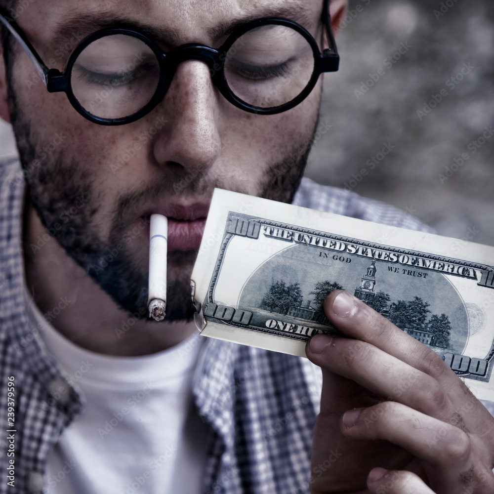 Young brutal businessman lighting cigarette with $100 dollar bill as a ...