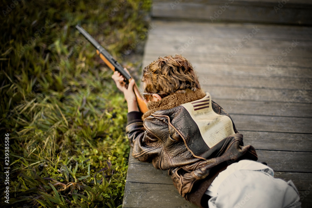 Boy aiming a shotgun while lying on his stomach on top of a wooden ...