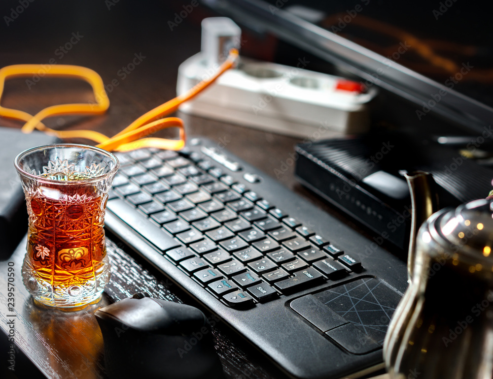 Crystal glass of black tea. Metal teapot. Black table. Black computer ...