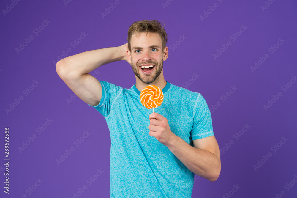 Man handsome macho eat big colorful sweet lollipop. Taste of childhood ...