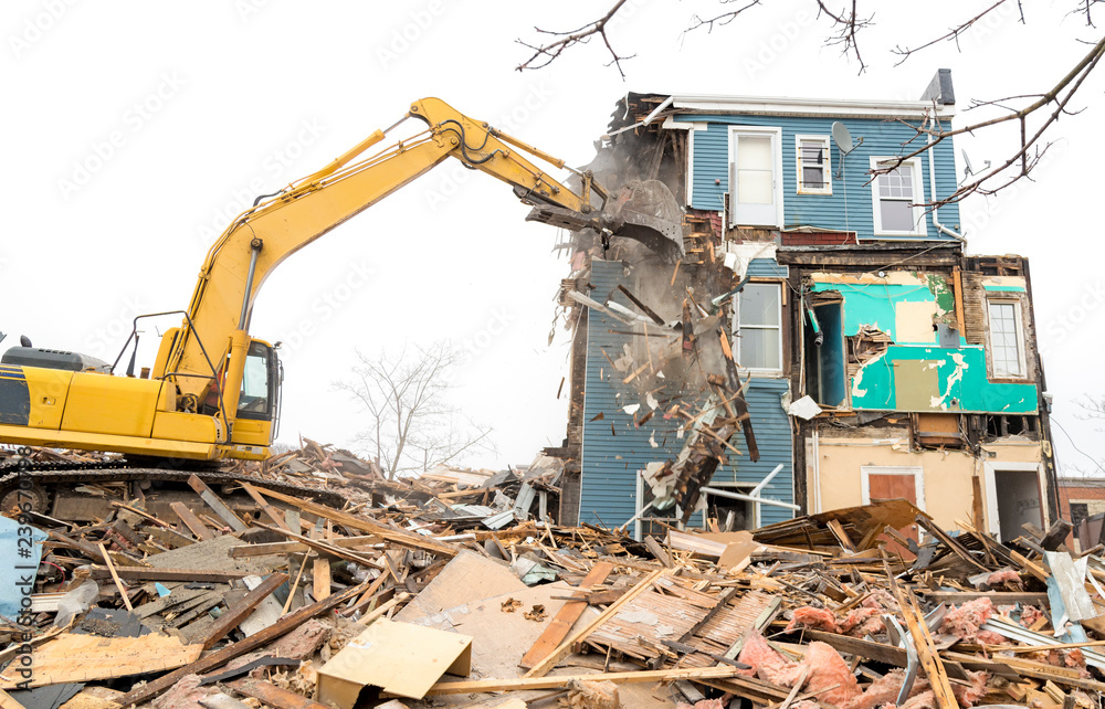Demolishing a building with a large backhoe. Overcast day. Air is dusty ...