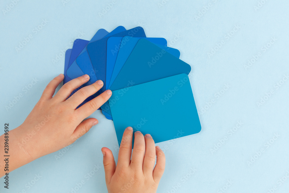 Child's hand playing with color sample cards - hues of blue. Top view ...