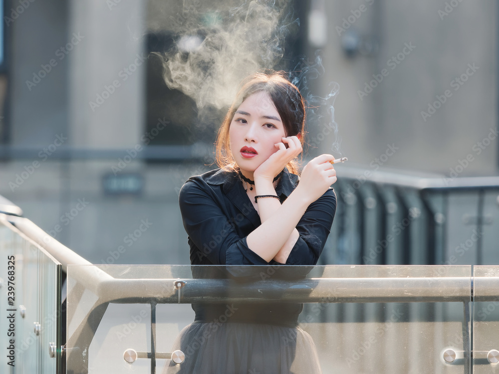 Portrait of beautiful Chinese girl in black dress smoking a cigarette ...