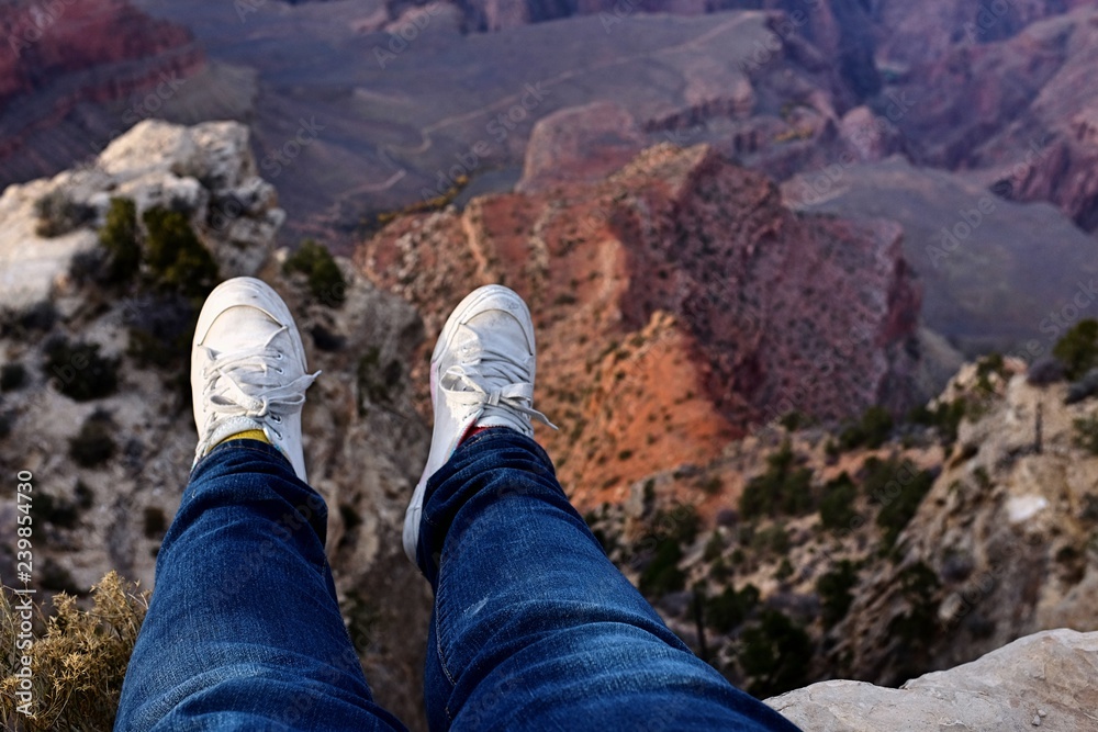 Feet dangle from the edge of a cliff, looking down into a valley in the ...