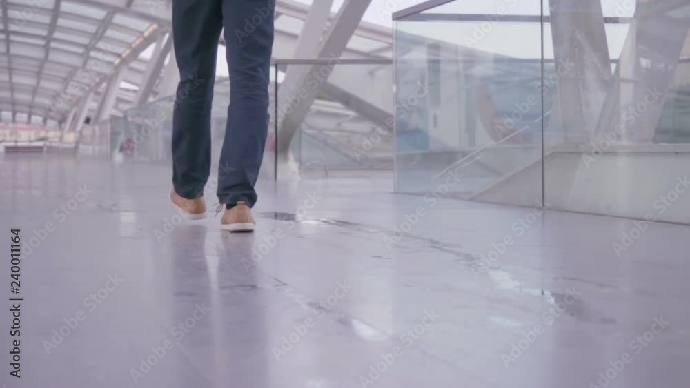 Stylish man walking in light corridor with glass walls, cropped view ...