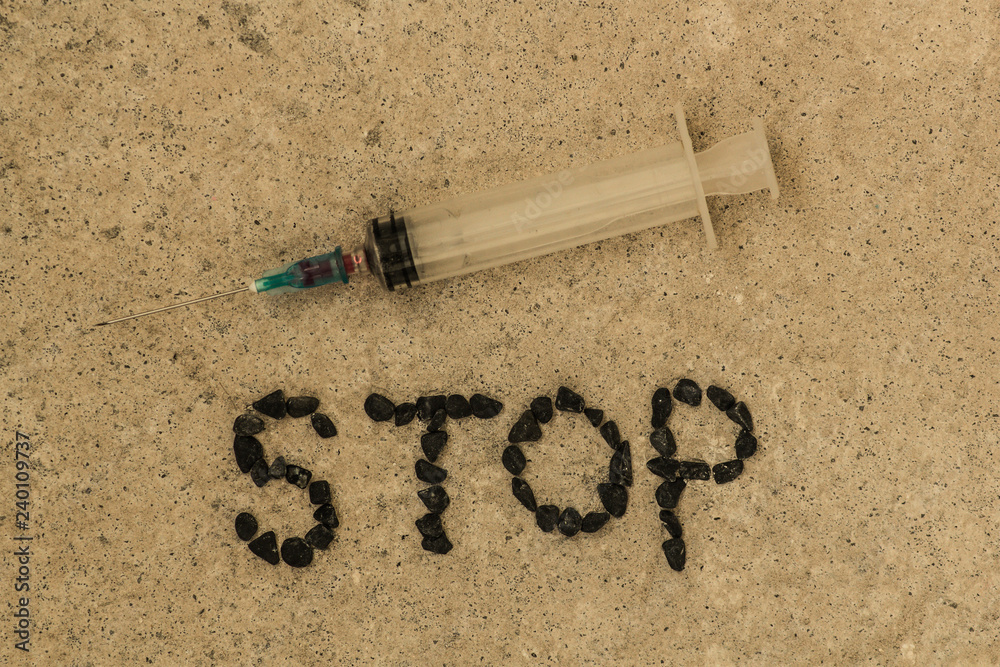 Syringe on a concrete floor and stop word from black stones. Anti drug ...