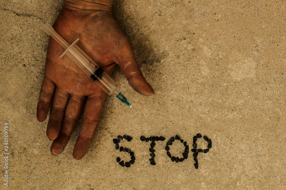 Hand of drug addicted with syringe and stop word on a grey cement ...