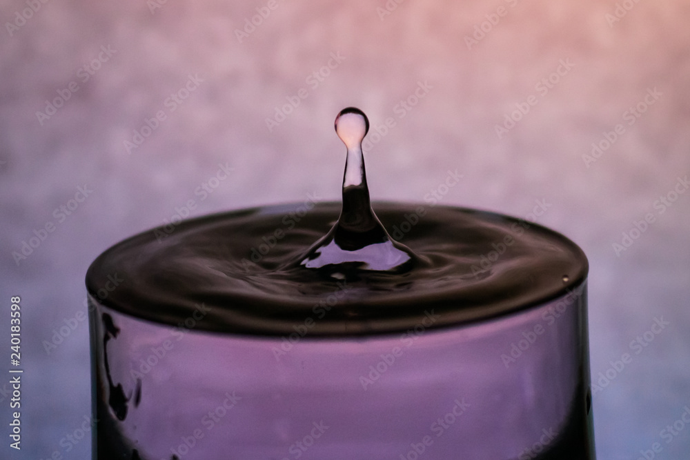 abstract water droplet hitting a full glass and creating a unique ...
