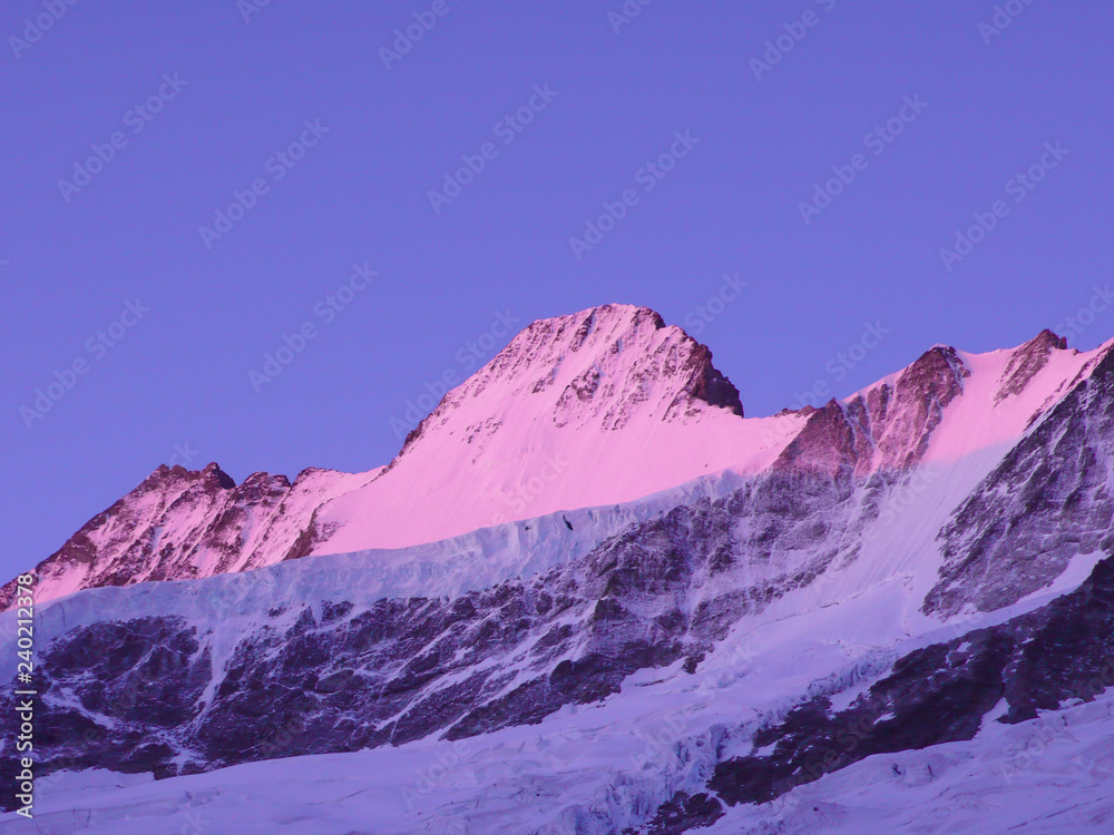 mountain climber on a steep and narrow snow ridge leading to a high ...