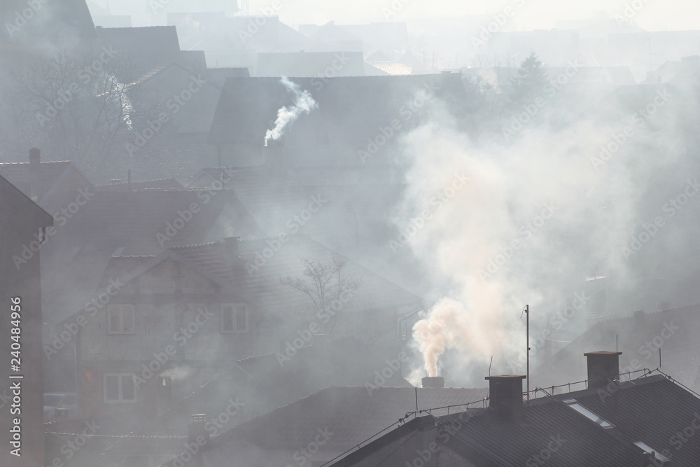Smoking chimneys at roofs of houses emits smoke, smog at sunrise ...