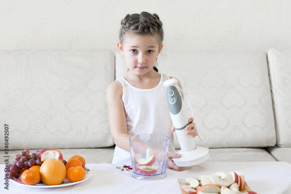 The child prepares a cocktail in a blender. A little girl prepares her ...