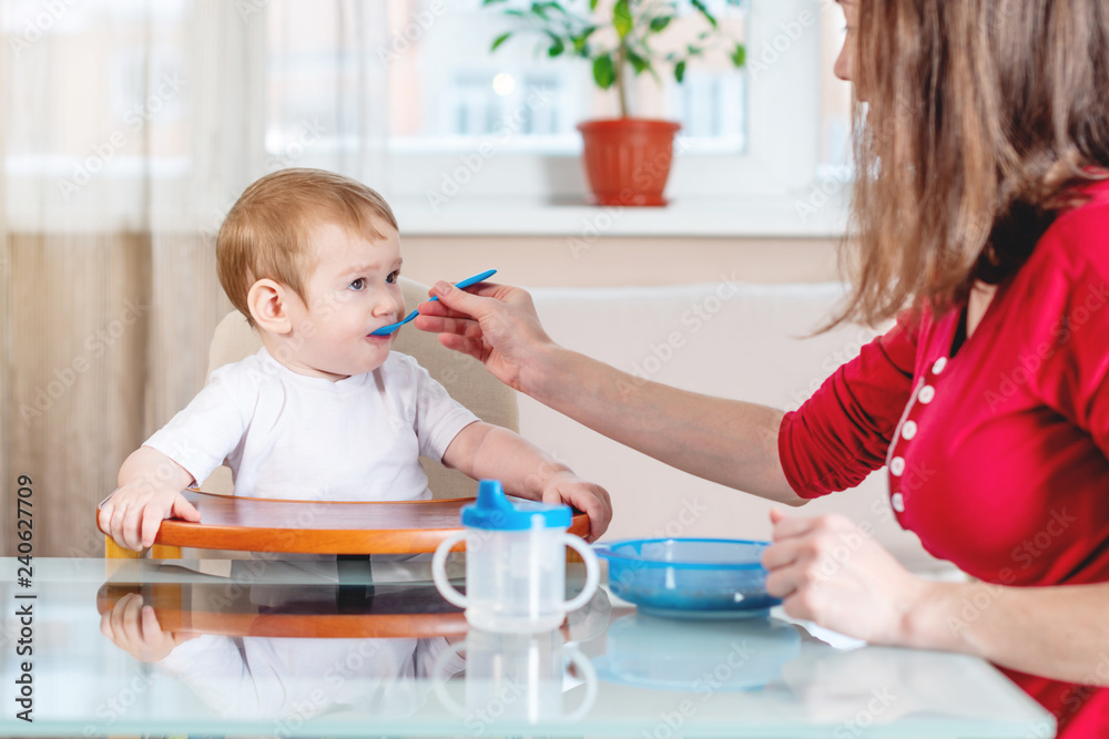 Mother feeding the baby holding out her hand with a spoon of porridge ...