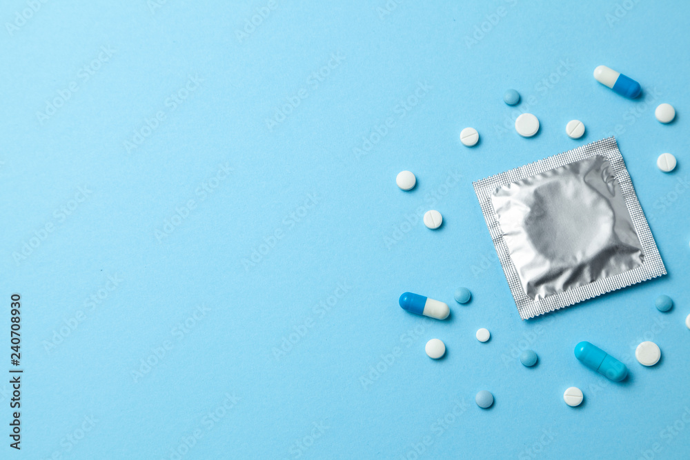 Birth control pills and condom in package on blue background. The ...