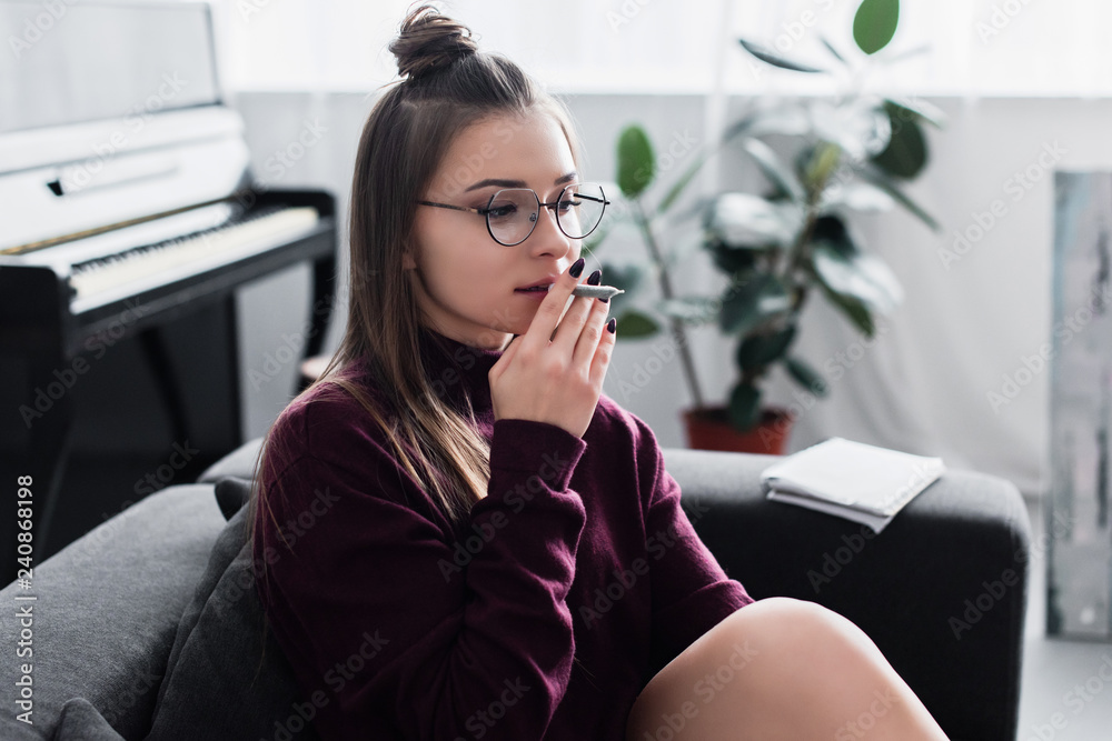 beautiful girl sitting on couch and smoking marijuana joint in living ...