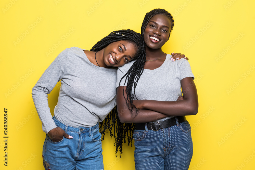 Portrait of two african young women hugging and laughing over yellow ...