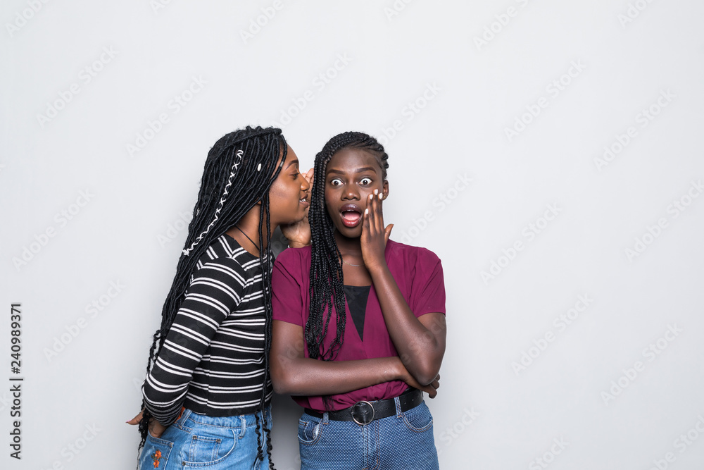 Portrait of two happy young african women sharing secrets isolated over ...