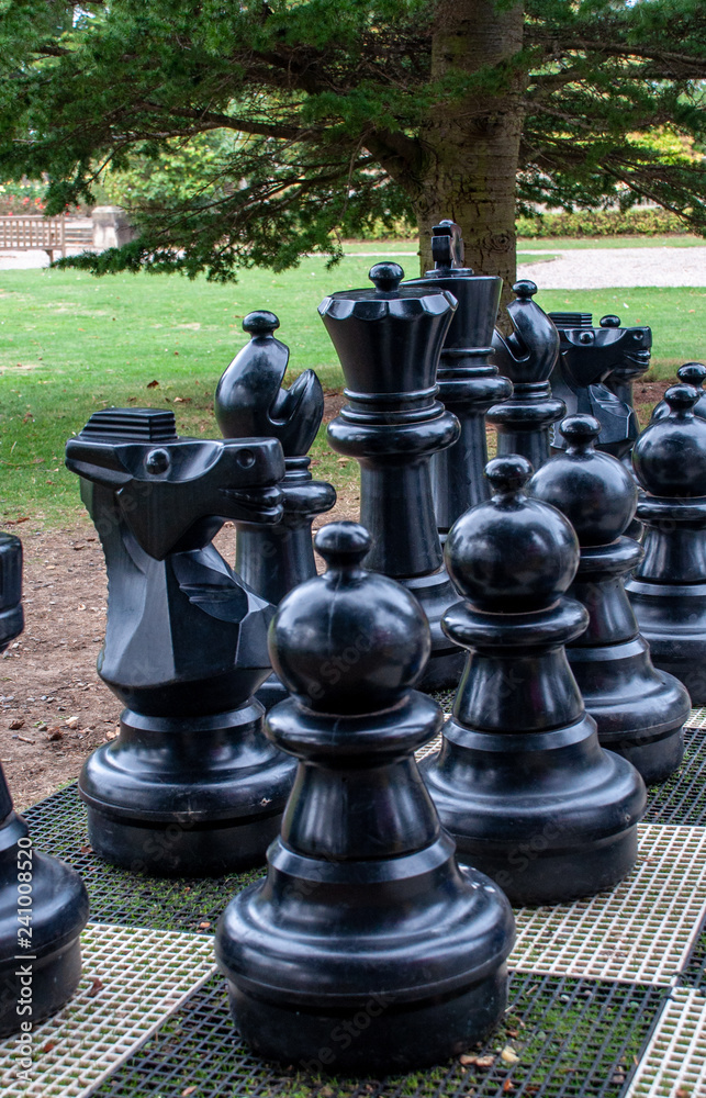 Black chess set, row of pieces outside on the giant chess board in a ...