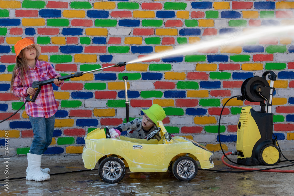 Happy girl with children washes yellow toy car from high pressure ...