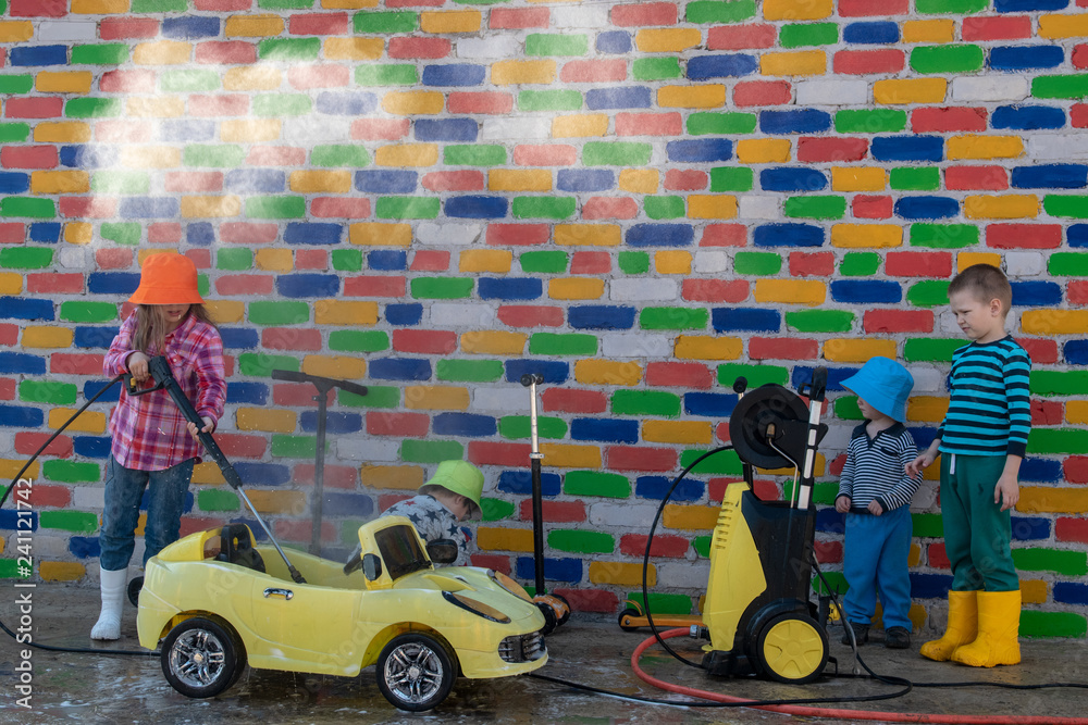 Happy girl with children washes yellow toy car from high pressure ...